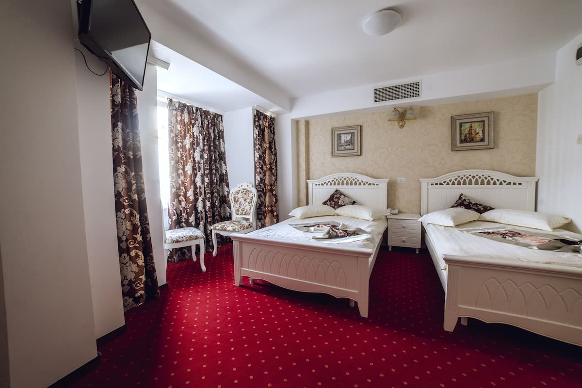 Quarto de hotel com duas camas, uma cadeira, uma televisão e um tapete vermelho.