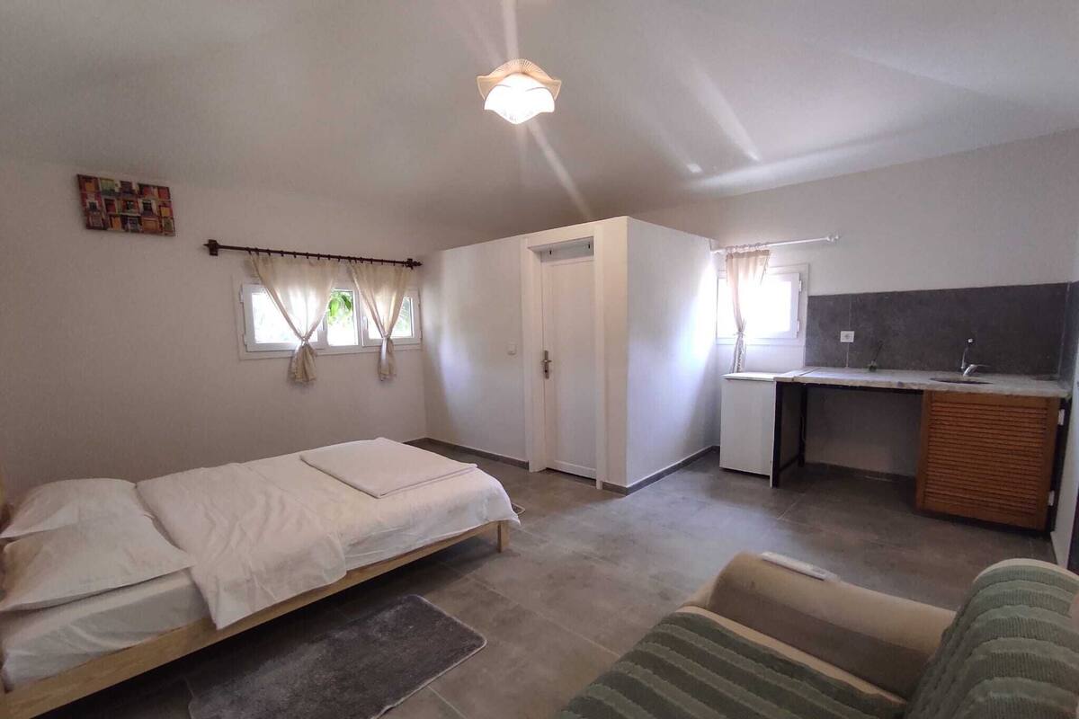 Quarto com cama, escrivaninha e cozinha compacta.