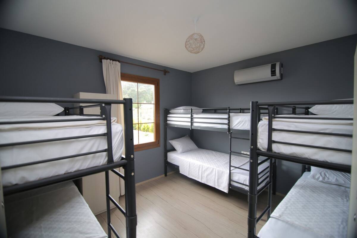 Um quarto de dormitório com beliches, uma janela com cortinas, um aparelho de ar condicionado e piso de madeira.
