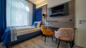 Quarto de hotel moderno com cama, escrivaninha, televisão e duas cadeiras.