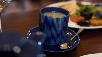 Uma mesa posta com uma chávena azul, uma colher e um prato com comida.