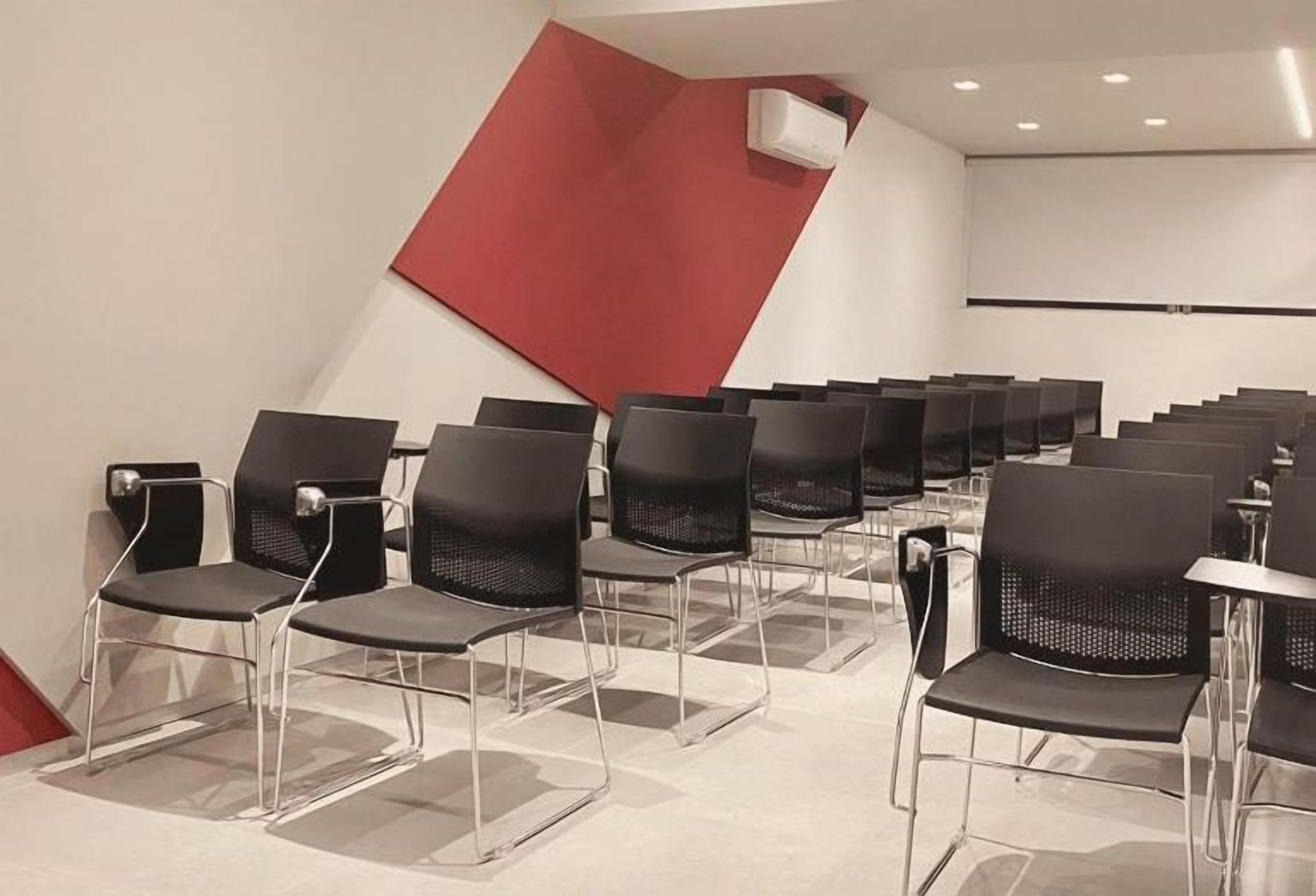 Uma sala de conferências no Verona Tower Hotel, com fileiras de cadeiras pretas e uma parede com detalhes em vermelho.