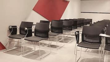 Uma sala de conferências no Verona Tower Hotel, com fileiras de cadeiras pretas e uma parede com detalhes em vermelho.
