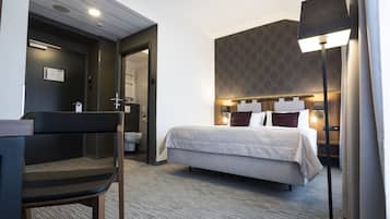 Quarto de hotel com cama, escrivaninha, cadeira, mesa de cabeceira, luminária e banheiro com vaso sanitário e pia.