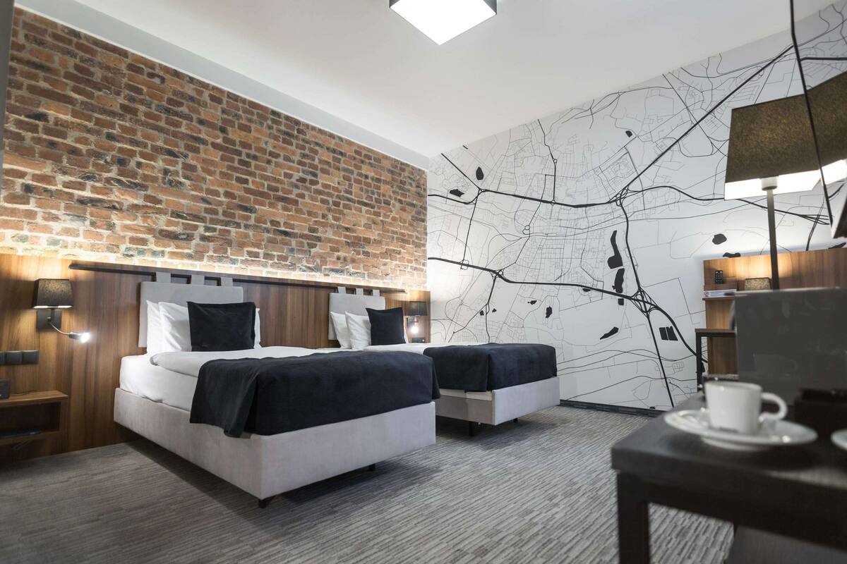 Quarto de hotel moderno com parede de tijolos, duas camas, um mural de mapa e uma mesinha de centro.