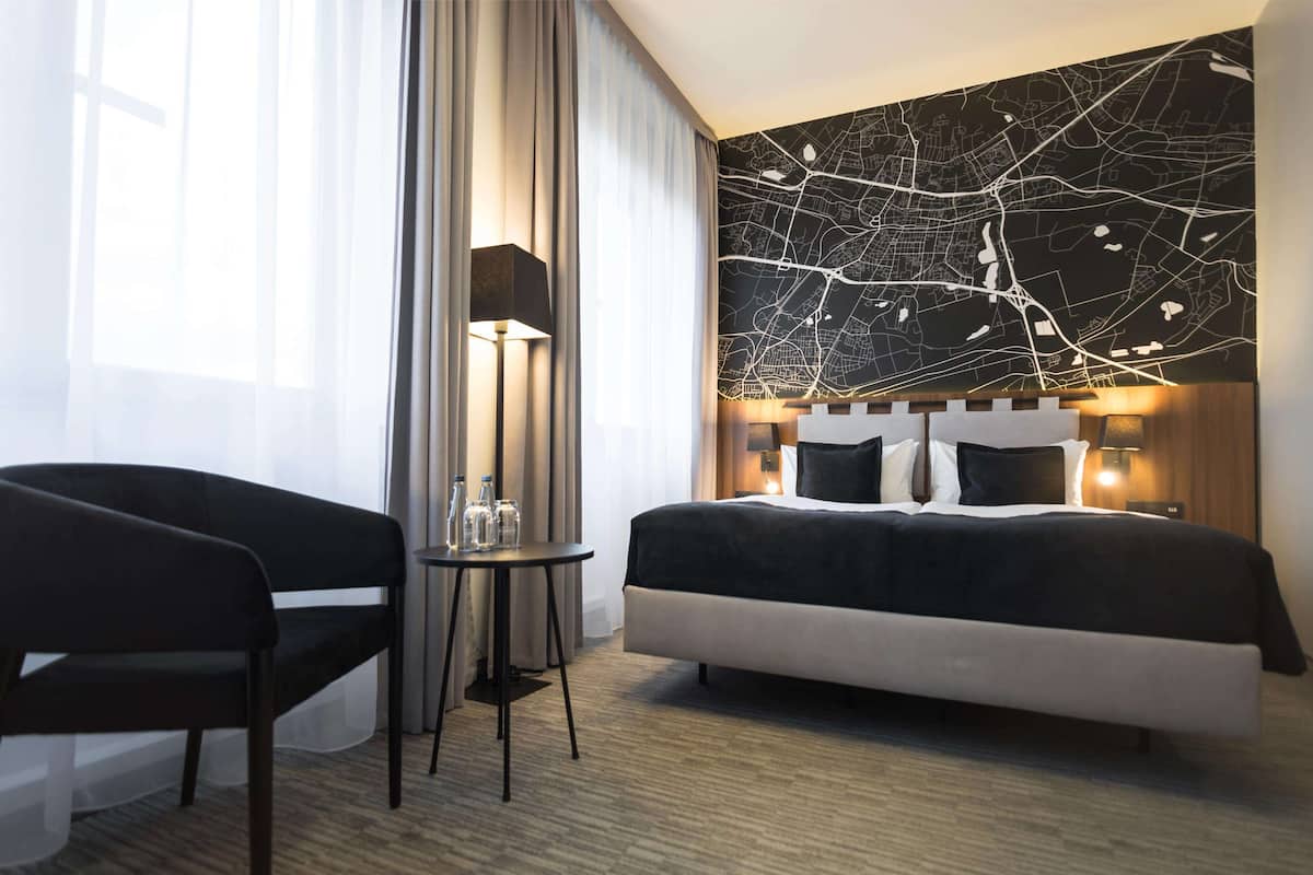 Quarto de hotel moderno com uma cama grande, uma escrivaninha, uma cadeira e um mural com um mapa na parede.