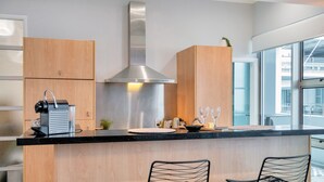 Cozinha moderna com armários de madeira, exaustor de aço inoxidável e bancada preta. Há duas cadeiras pretas e uma pequena planta na bancada.