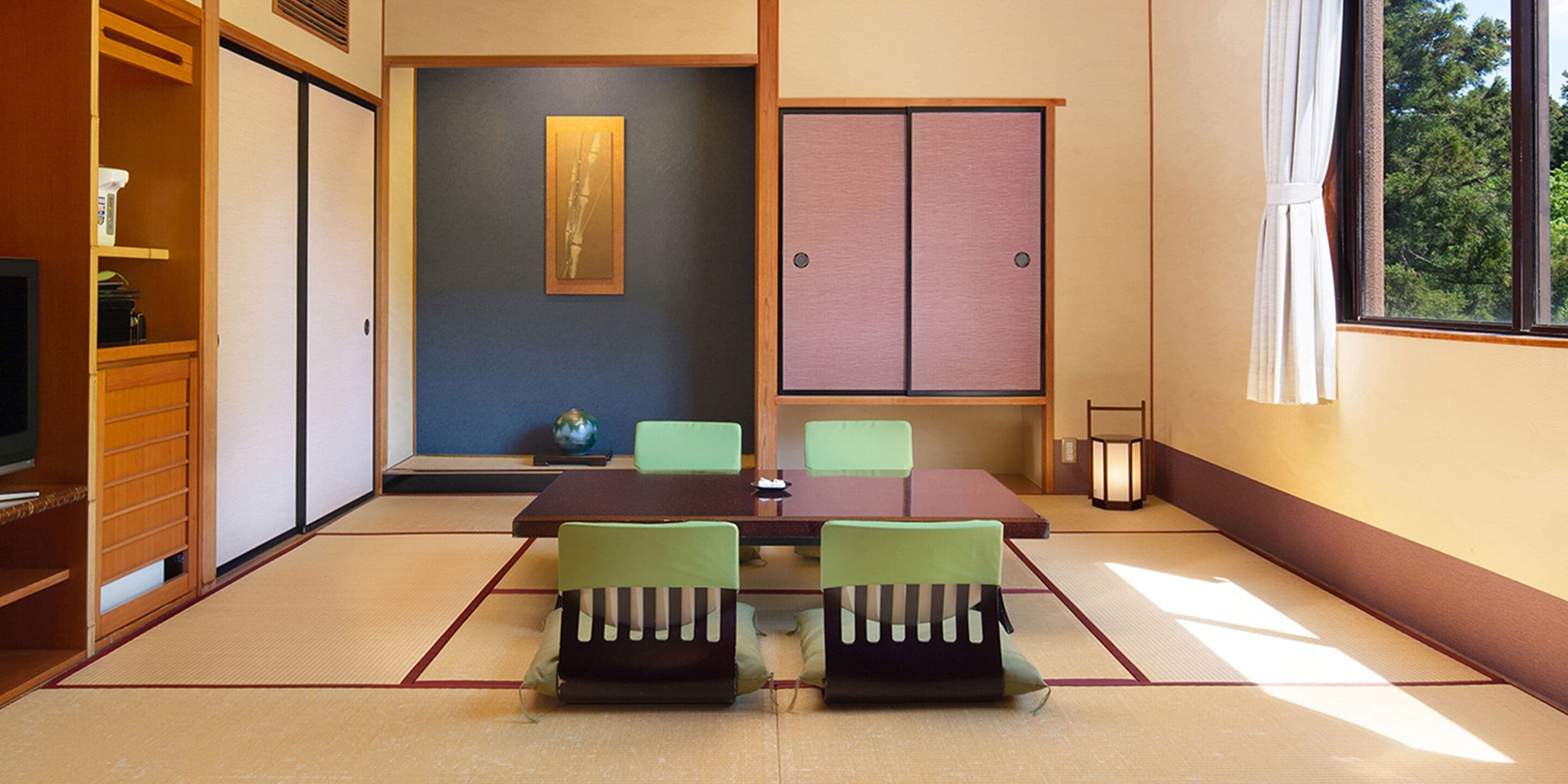 Um quarto japonês tradicional com tatames, uma mesa baixa, duas cadeiras verdes, um armário e uma porta deslizante.