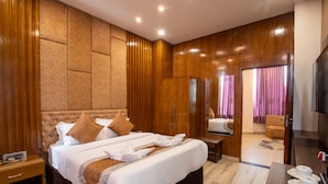 Quarto de hotel com cama grande, painéis de madeira, espelho, televisão e uma pequena mesa com xícaras.