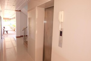 Um corredor limpo e moderno, com um elevador brilhante e um telefone na parede.
