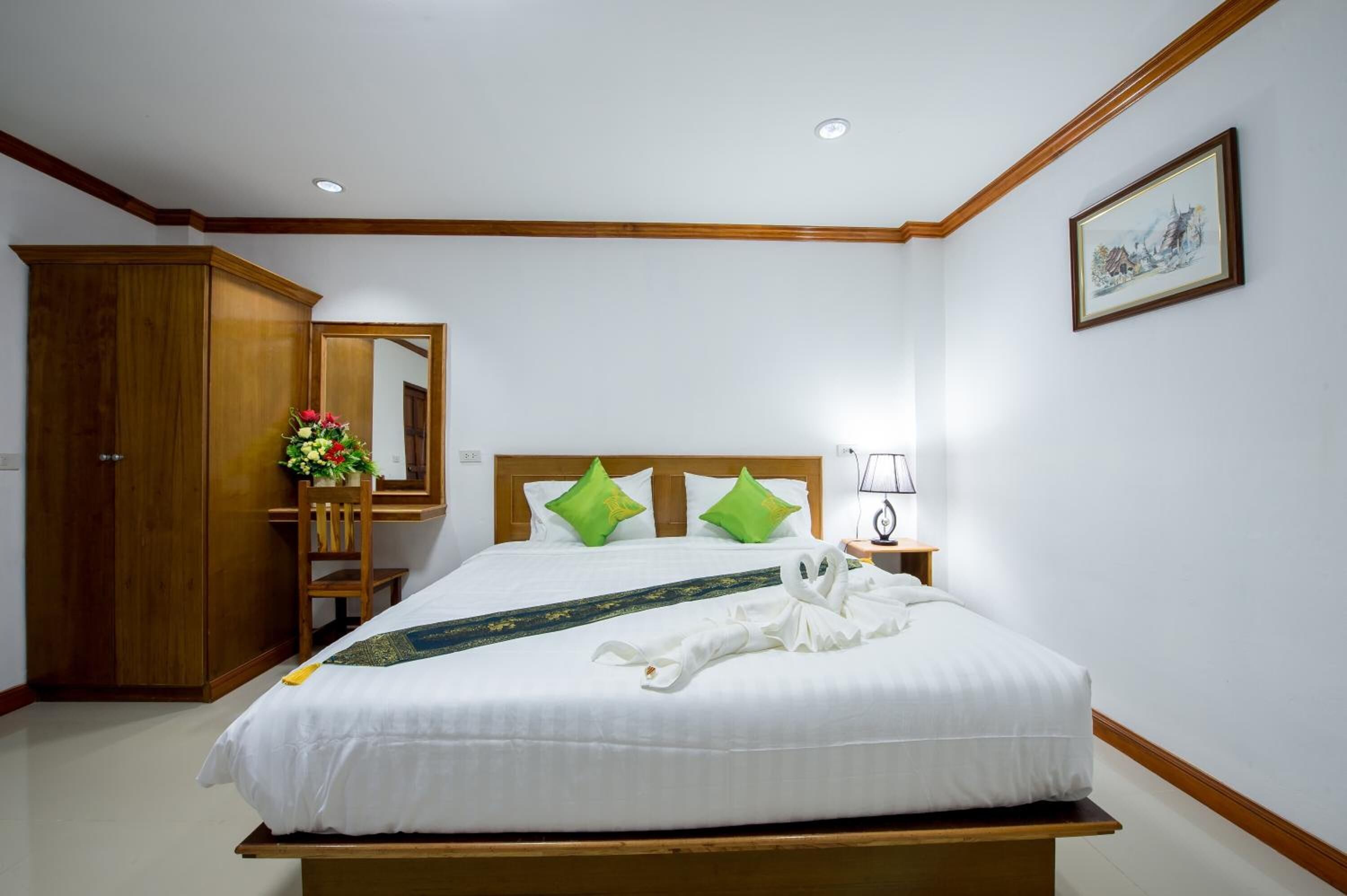 Quarto de hotel com cama grande, cabeceira de madeira, travesseiros verdes, guarda-roupa de madeira, espelho e um quadro na parede.