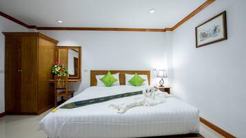 Quarto de hotel com cama grande, cabeceira de madeira, travesseiros verdes, guarda-roupa de madeira, espelho e um quadro na parede.