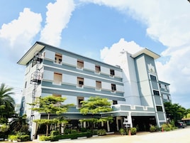 Um hotel de vários andares com fachada azul clara, várias varandas e uma área de entrada coberta com vegetação.