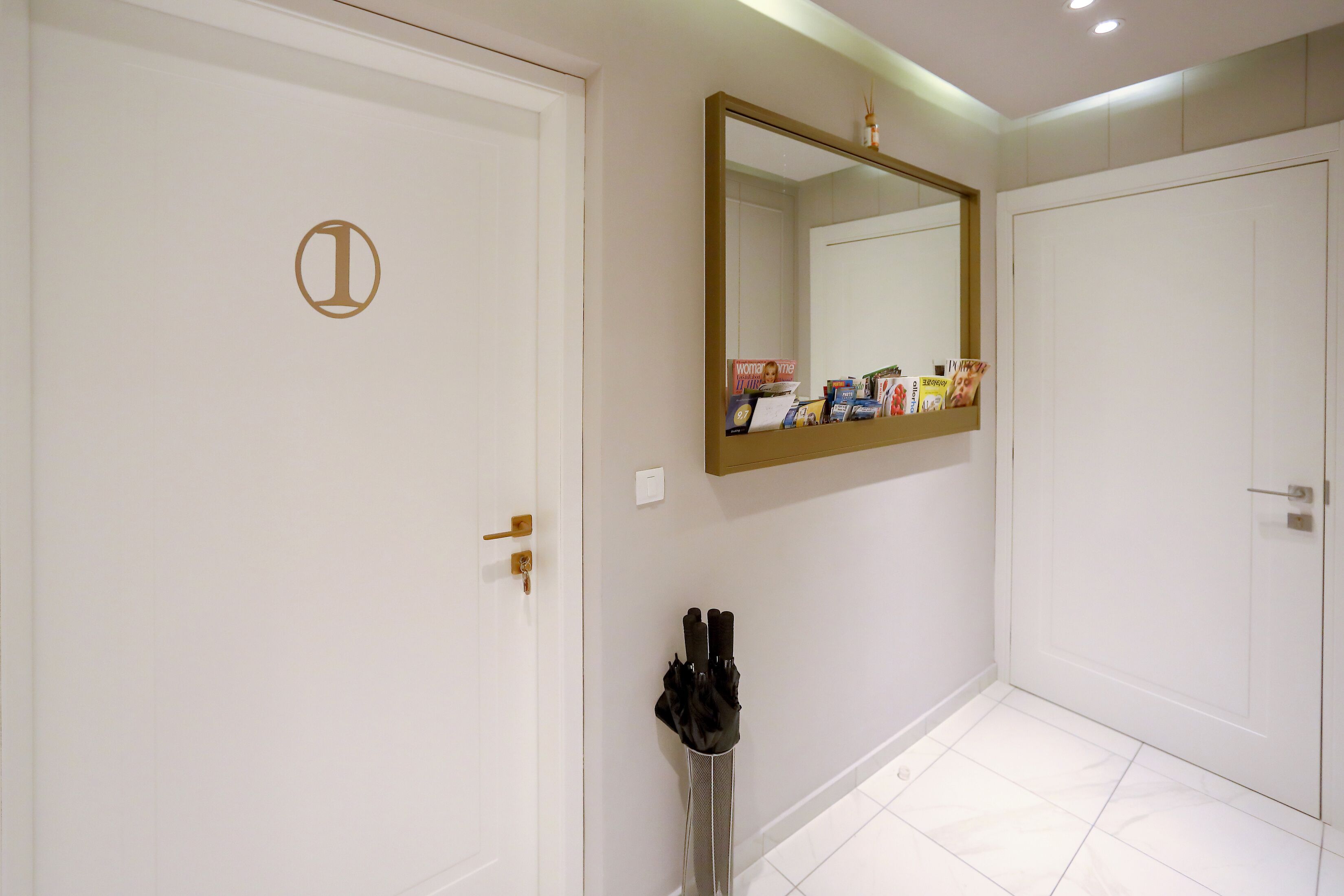 Um corredor com portas brancas, um espelho e um suporte para guarda-chuvas.