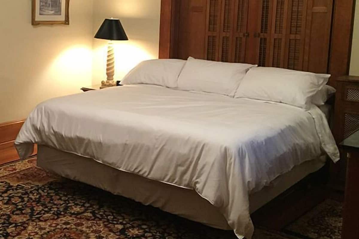 Um quarto com cama, uma cadeira, uma mesinha e uma luminária.