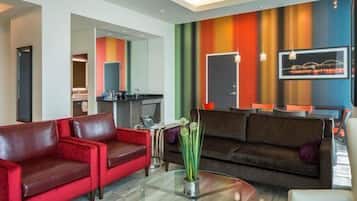 Um hall de hotel com um sofá vermelho, um sofá marrom, uma mesa de centro de vidro e uma parede colorida.