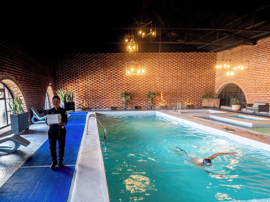 Piscina interior com parede de tijolos, salva-vidas e um nadador.
