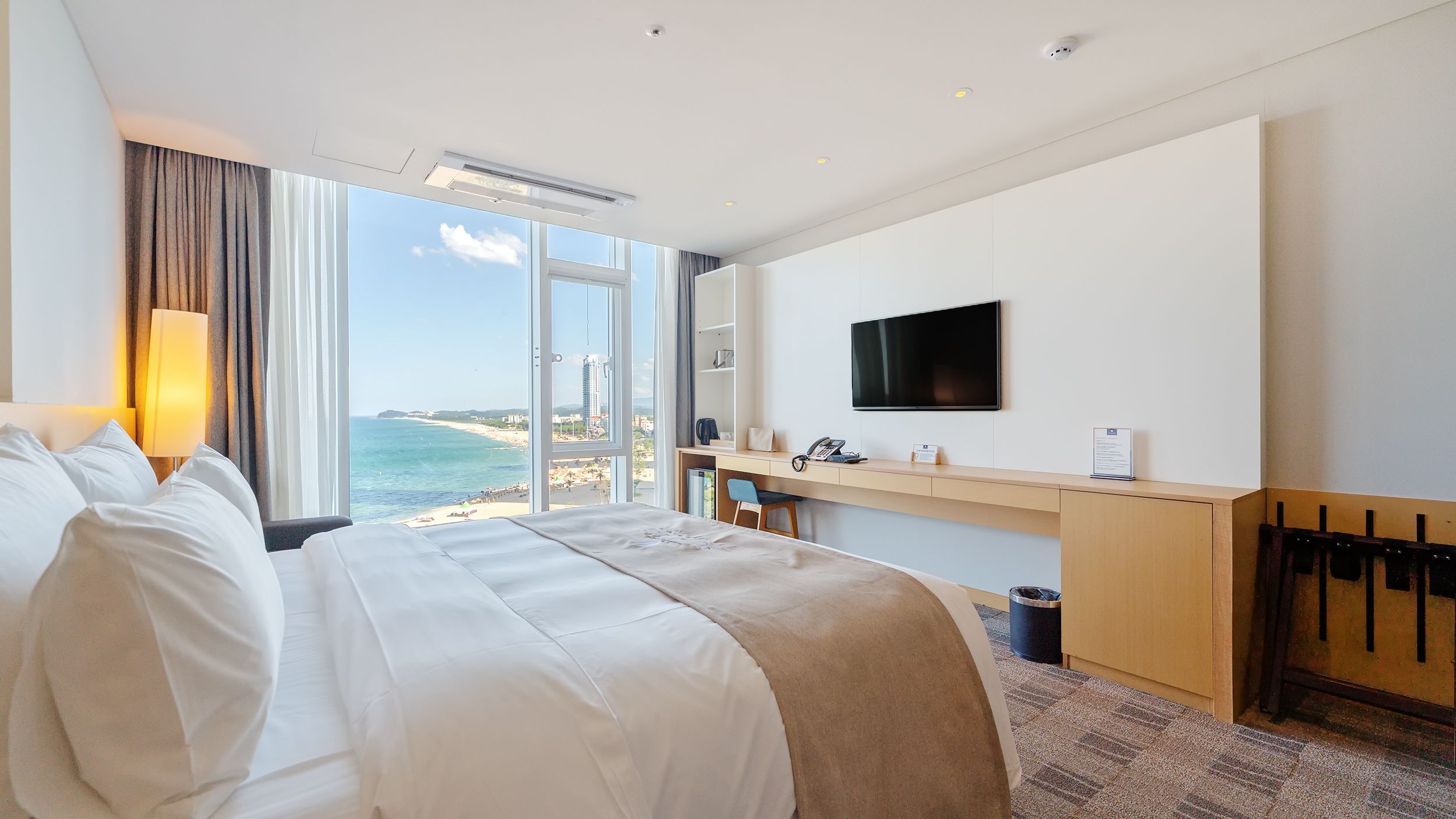 Quarto de hotel com cama, escrivaninha, televisão e vista para a praia.