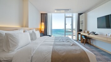 Quarto de hotel com cama, escrivaninha, televisão e vista para o mar.