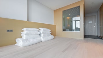 Quarto com piso de madeira, parede bege e uma grande janela com persianas.
