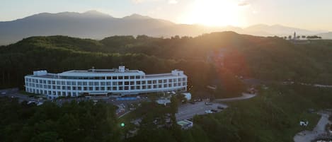 Um edifício moderno com design circular, cercado por vegetação exuberante e montanhas ao fundo.