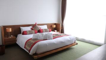 Quarto de hotel com uma cama grande, duas mesas de cabeceira, um abajur e uma janela com cortinas.