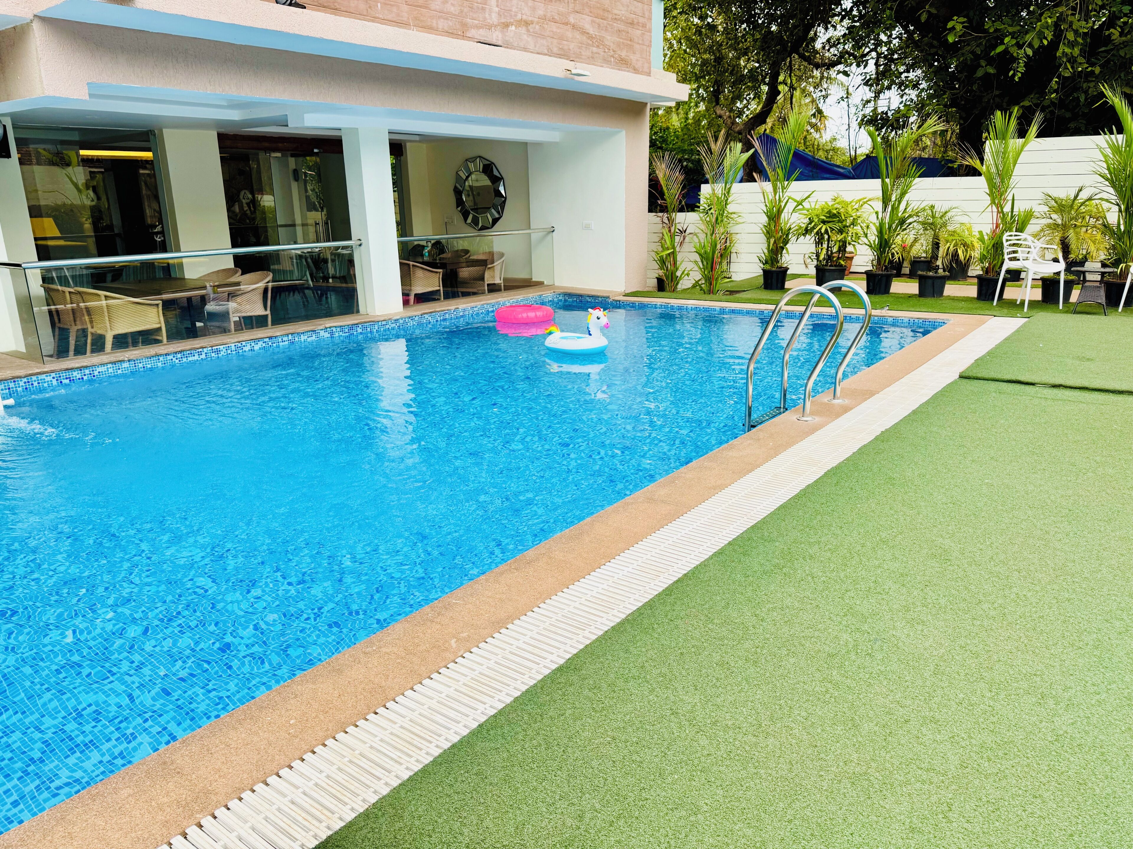 Uma piscina com água azul cristalina, rodeada por um gramado artificial verde e um guarda-corpo branco.