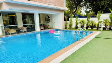Uma piscina com água azul cristalina, rodeada por um gramado artificial verde e um guarda-corpo branco.