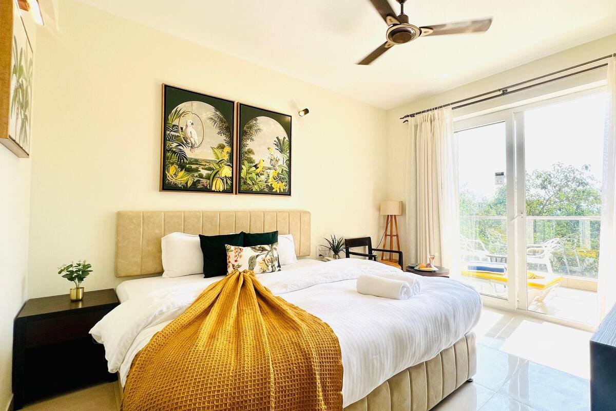 Quarto com cama, mesa de cabeceira, abajur, ventilador de teto e varanda com mobiliário.