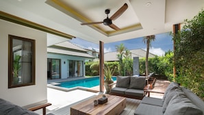Uma sala de estar moderna com vista para a piscina, um ventilador de teto e uma mesa de centro de madeira.