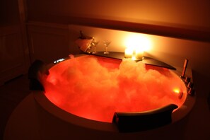 Uma banheira de hidromassagem com luz vermelha, um copo e uma vela.