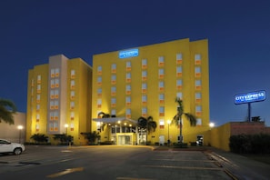 Um hotel com vários andares e um letreiro chamativo 'CITY EXPRESS BY MARIE', um estacionamento e uma entrada bem iluminada.