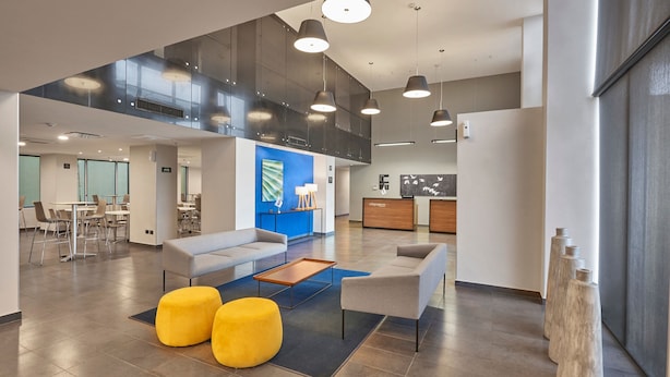 Um hall espaçoso com teto alto, móveis modernos e uma área de estar central com pufes amarelos.