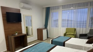 Quarto de hotel com duas camas, uma escrivaninha, televisão, minibar e janela com cortinas.