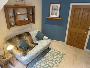 Um quarto com um sofá estampado, um armário de madeira com louças, um quadro emoldurado e uma porta.