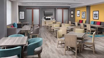 Um hall de hotel com várias áreas de estar, incluindo sofás e mesas, um bar e uma televisão de tela plana na parede.