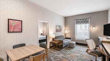 Quarto de hotel com mesa de jantar, duas cadeiras, sofá, televisão e janela com vista.