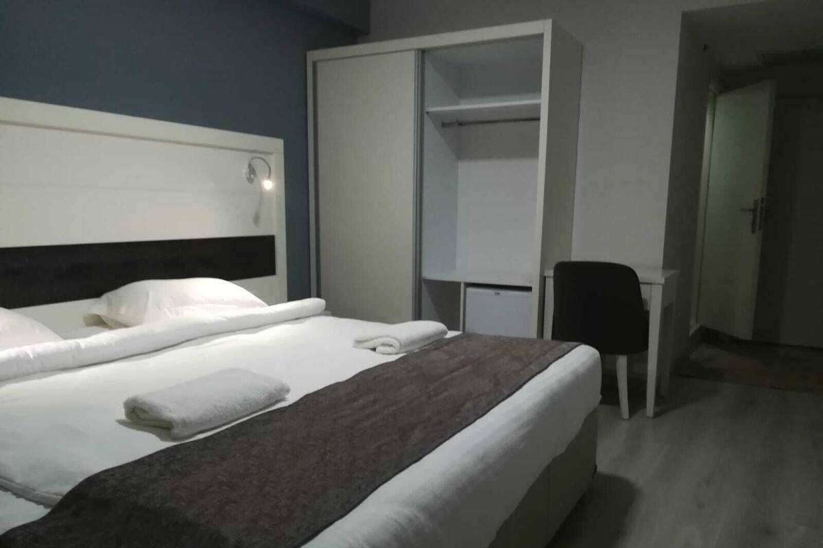 Quarto de hotel com cama, guarda-roupa e secretária.