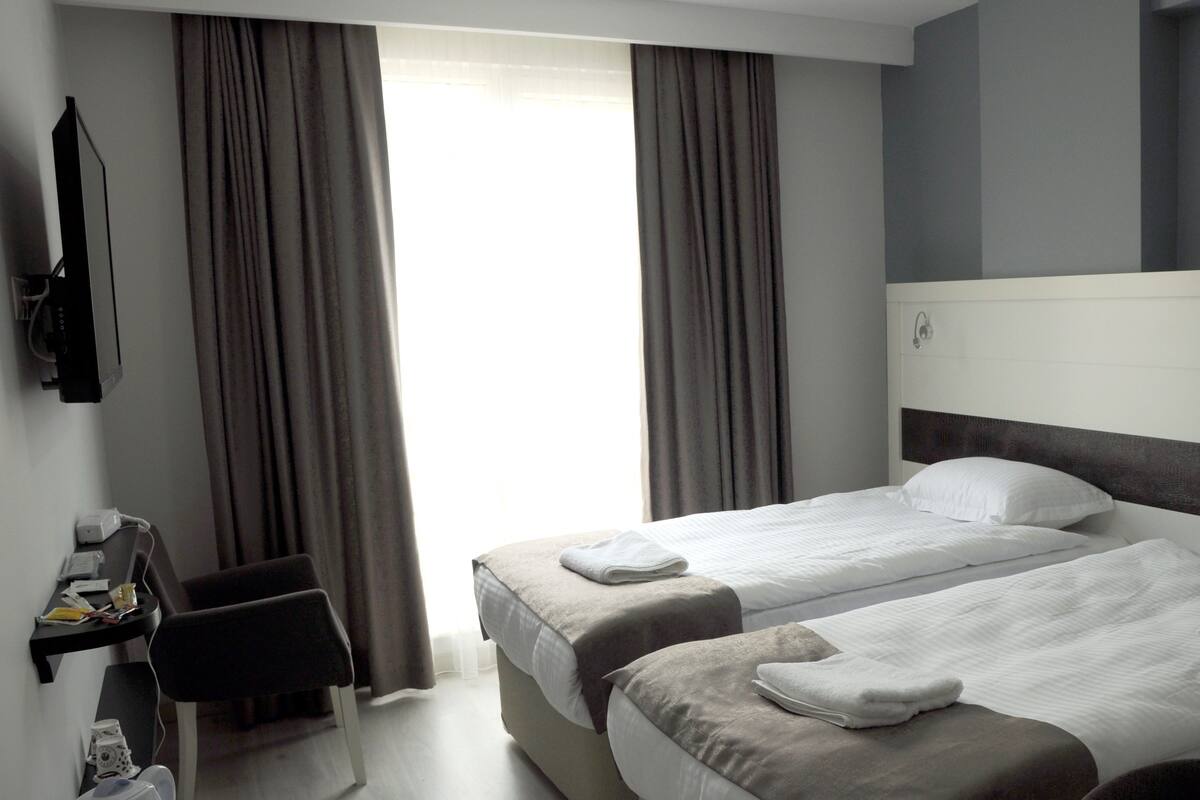 Quarto de hotel com duas camas, uma escrivaninha, uma cadeira e uma televisão.