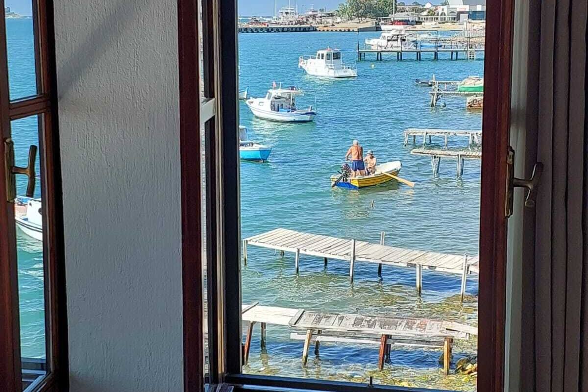 Vista de um quarto com janela aberta, dando para uma marina com barcos e cais.