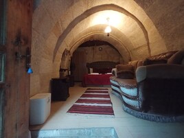 Um quarto acolhedor com porta de madeira, colcha vermelha, tapete estampado e sofá de couro.