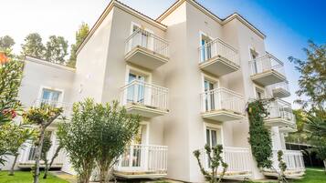 Edifício residencial com várias andares e varandas, rodeado por vegetação.
