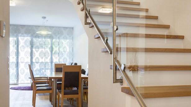 Um interior moderno com escada de madeira, área de refeições com cadeiras e mesa, e cortinas estampadas.