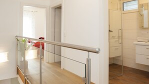Interior moderno com escada de madeira, guarda-corpo de vidro e banheiro com chuveiro e espelho.