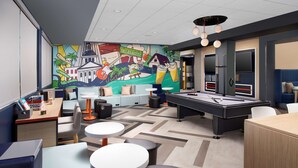 Uma área de estar moderna com mesa de bilhar, assentos confortáveis e um mural colorido na parede.