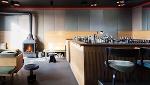 Uma área de bar moderna com lareira a lenha, banquetas e diversos frascos no balcão.