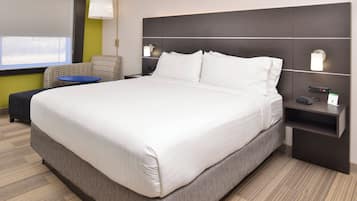Quarto de hotel com uma cama grande, uma mesa pequena, uma cadeira, uma mesa de cabeceira com abajur e vista para o exterior.