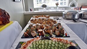 Uma mesa de buffet com diversos pratos, incluindo um centro com carne assada, frutos do mar e legumes frescos.