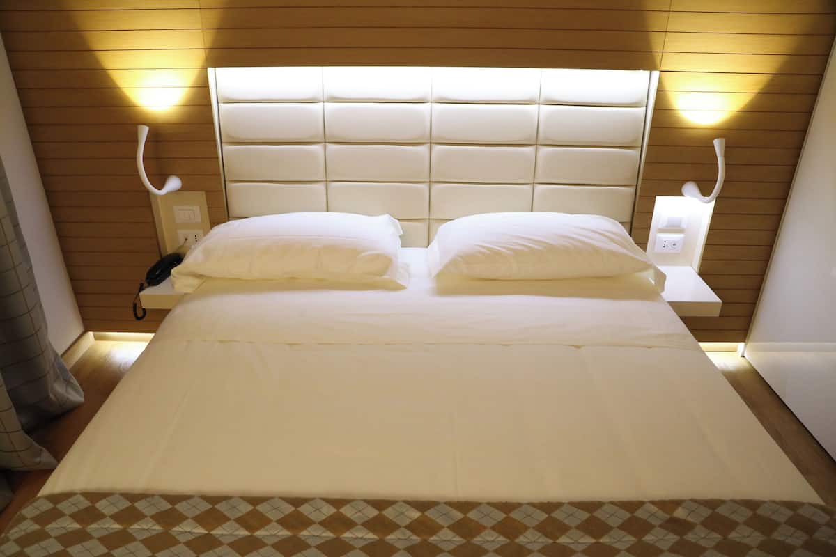 Uma cama bem arrumada com cabeceira, duas luminárias de apoio e um telefone em uma mesinha de cabeceira.