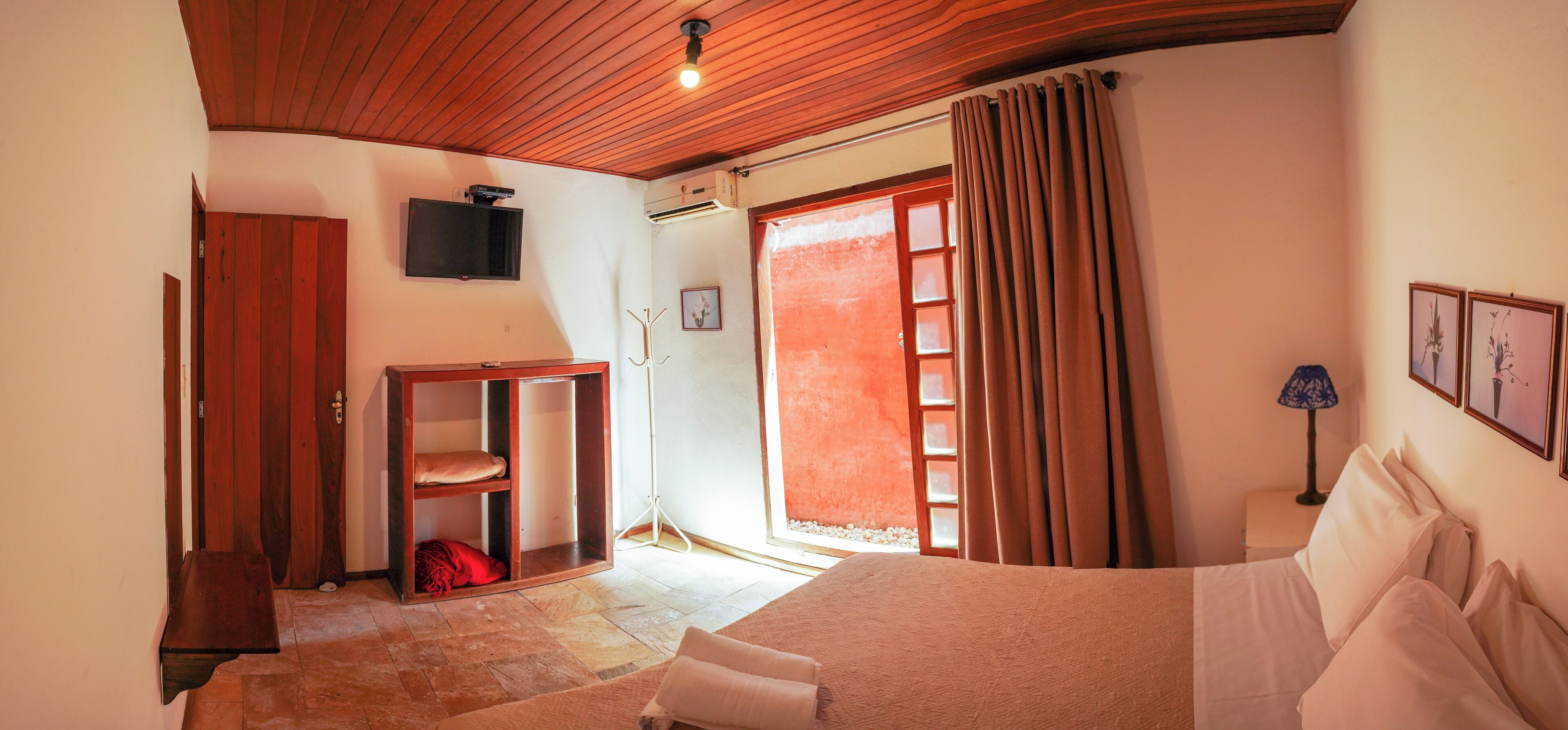 Quarto com cama, guarda-roupa de madeira, televisão e janela com cortinas.